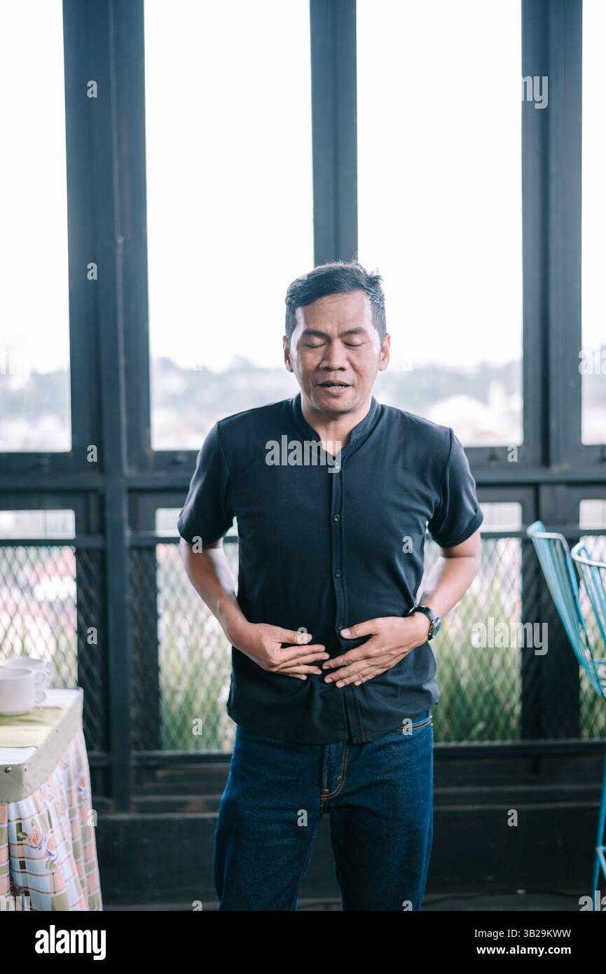 An older man holds his abdomen, portraying stomach issues in a casual ...