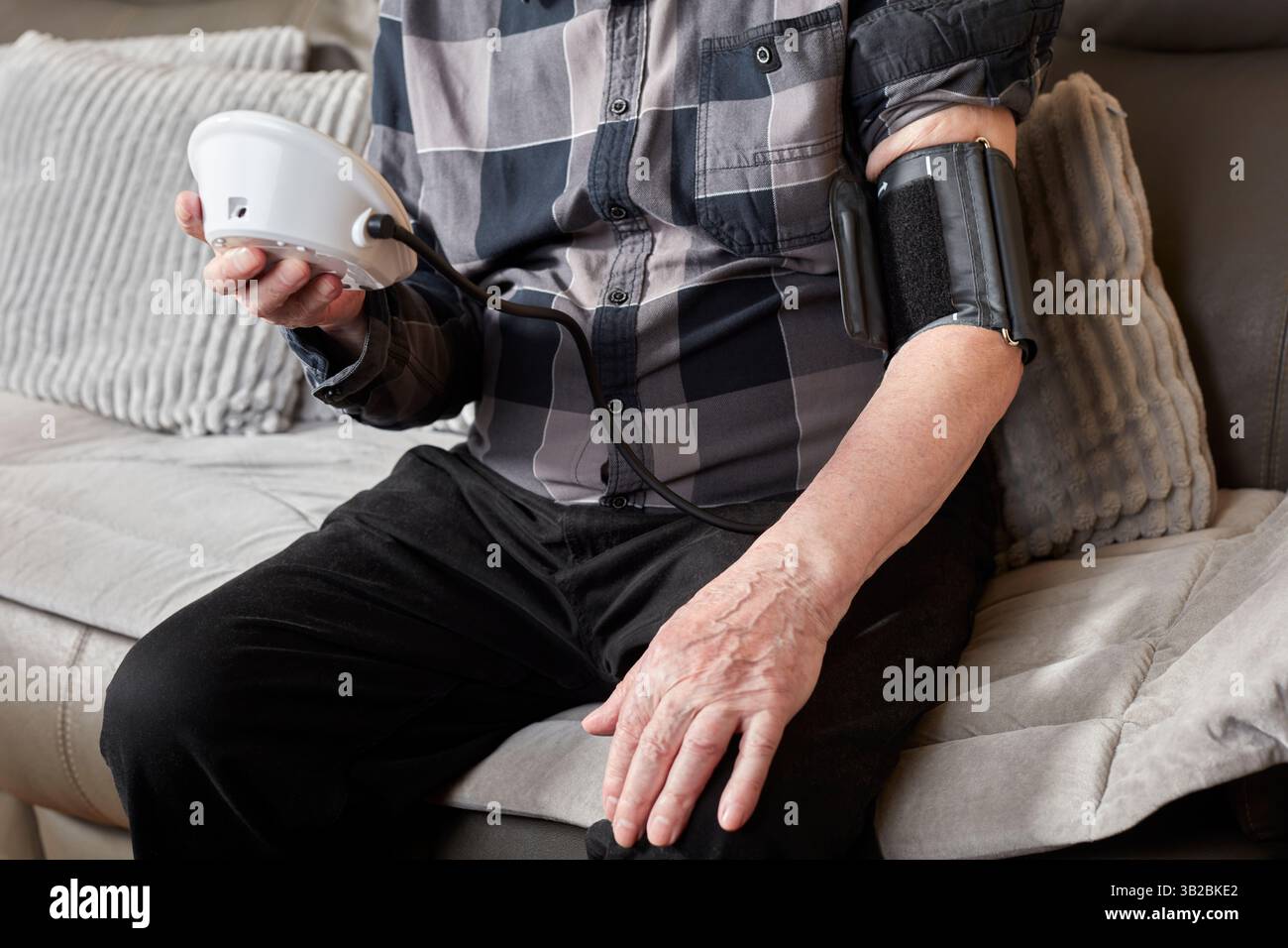 An elderly person sits on a sofa, using a home blood pressure monitor ...