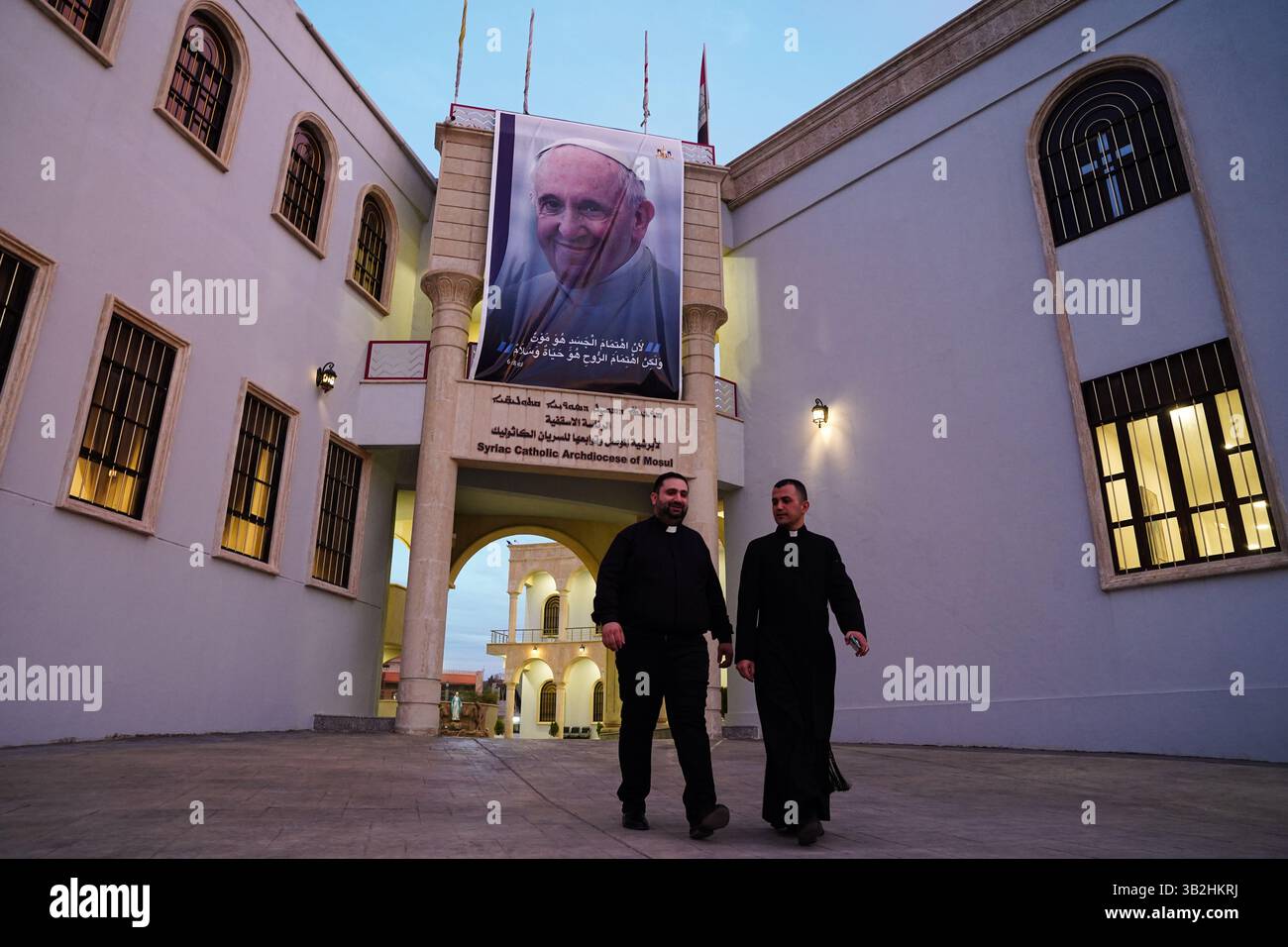 Al Hamdaniya, Iraq. 27th Apr, 2025. Priests walk under the picture of ...