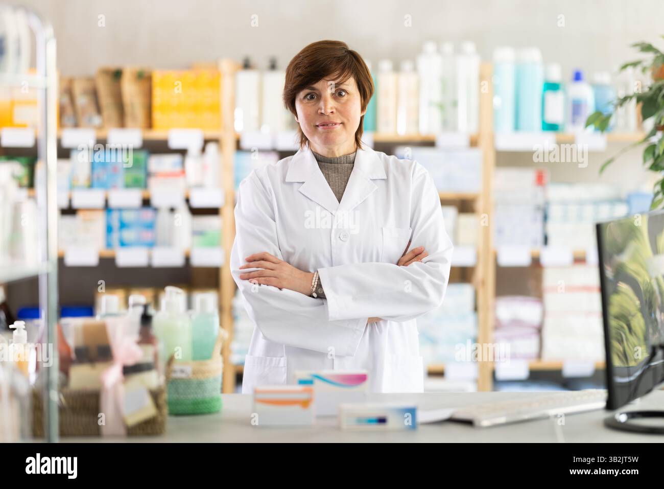 Confident female pharmacist standing behind counter with arms crossed ...