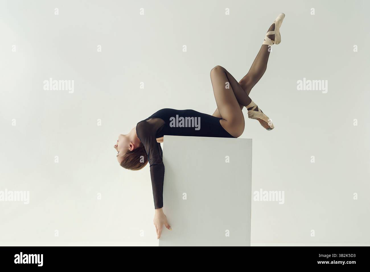 a ballerina in a black bodysuit lies on a cube with her head thrown ...