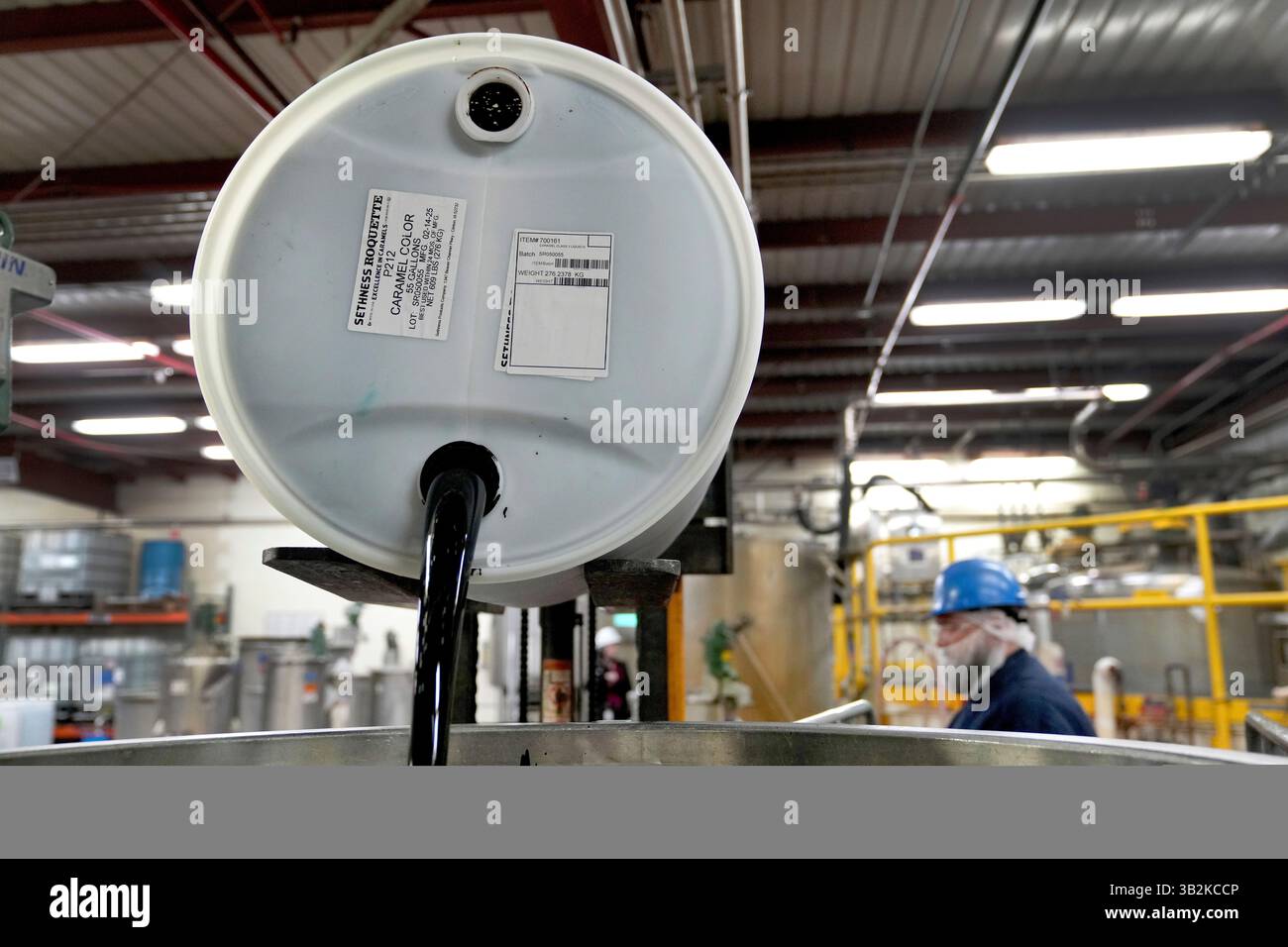 A container of caramel coloring is poured into a vat to be mixed before ...