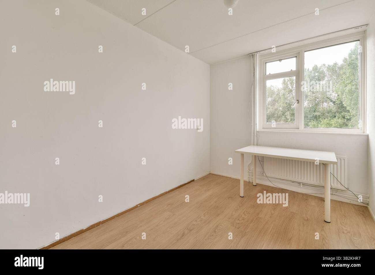 A spacious, empty room with white walls and a simple table. Natural ...