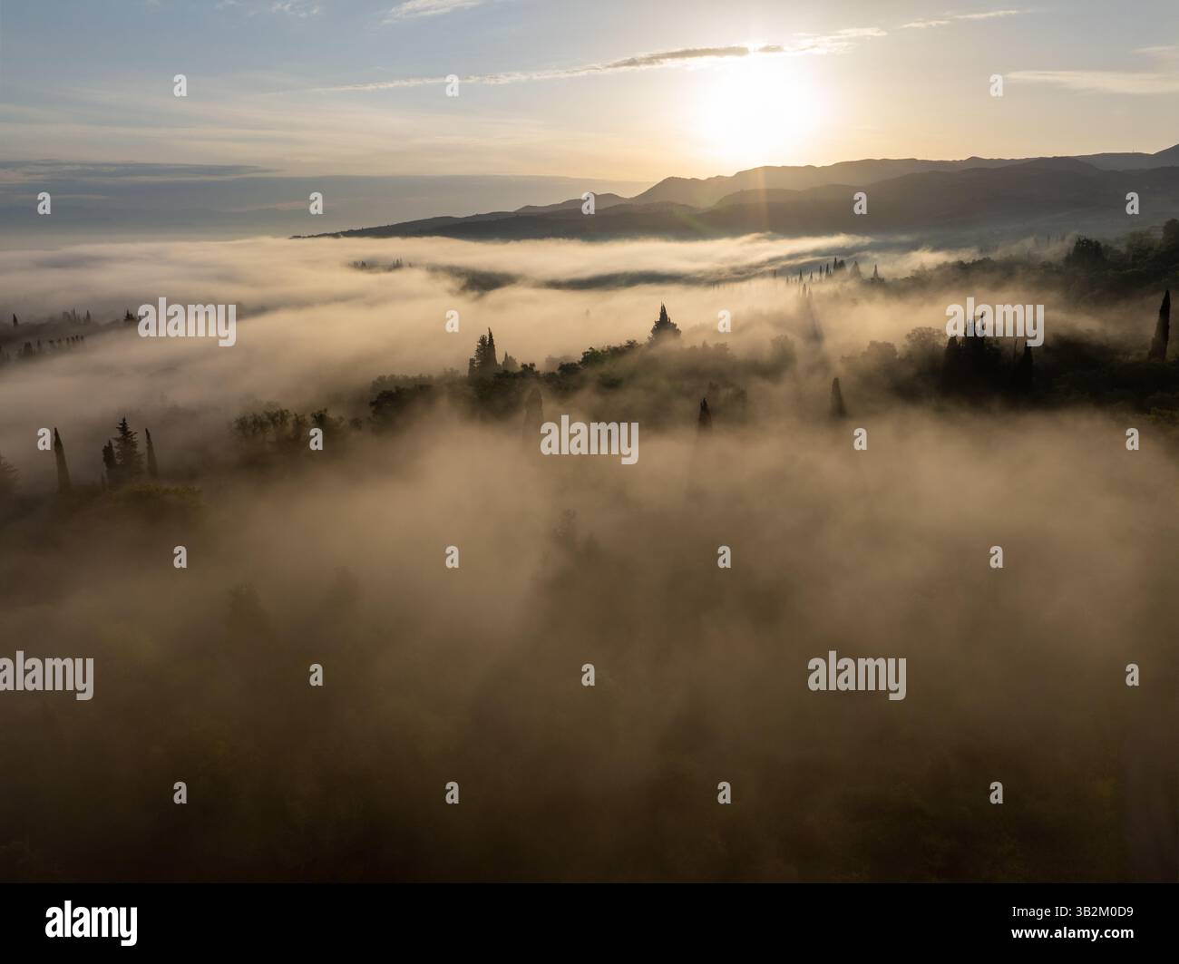 Misty sunrise over a valley filled with fog, casting long shadows and a ...