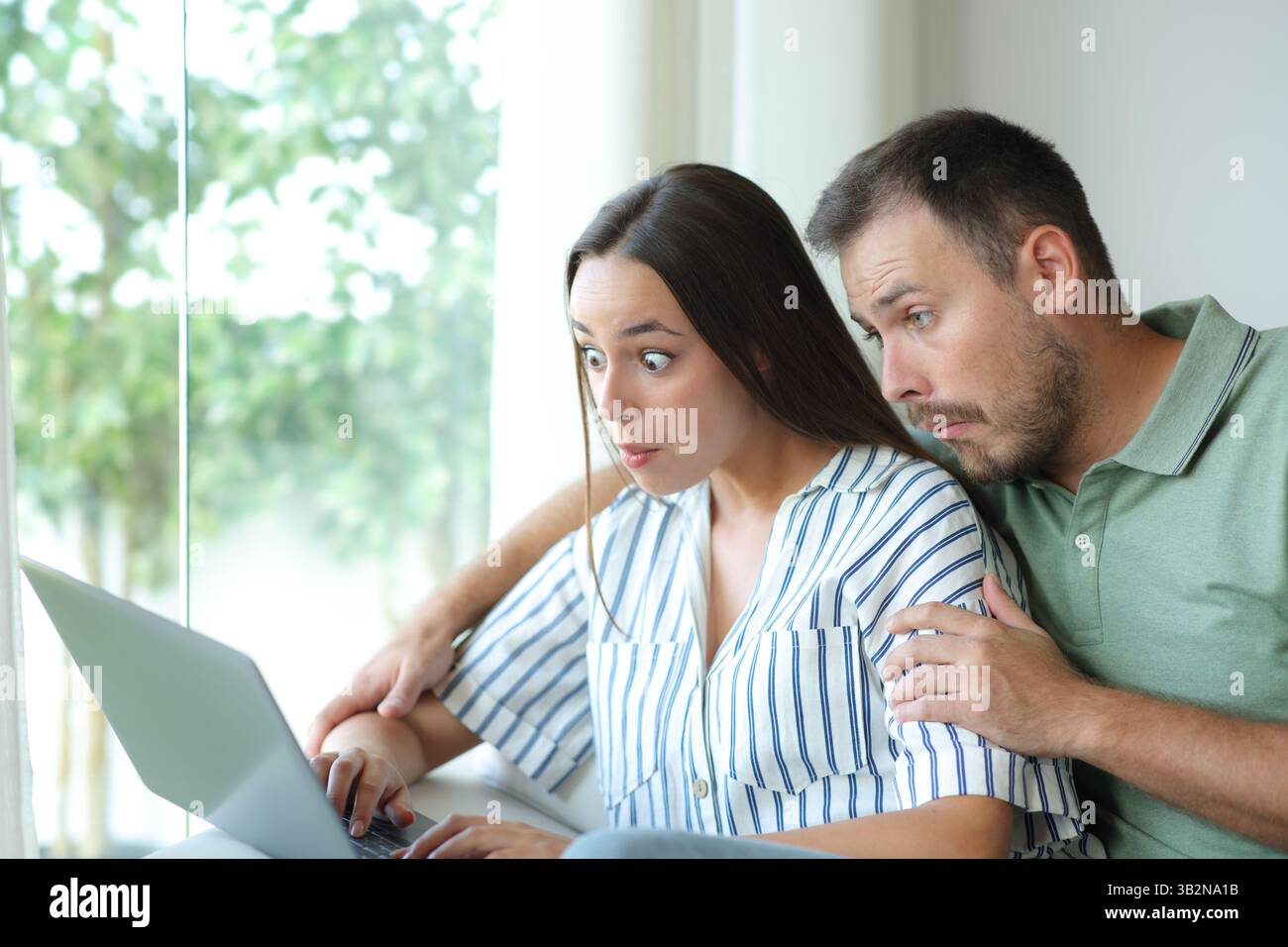 Perplexed couple checking absurd laptop content sitting on a couch at ...