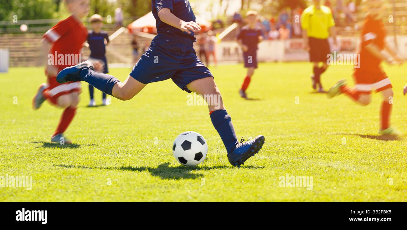 Children playing soccer in a match, with a player in blue kicking the ...