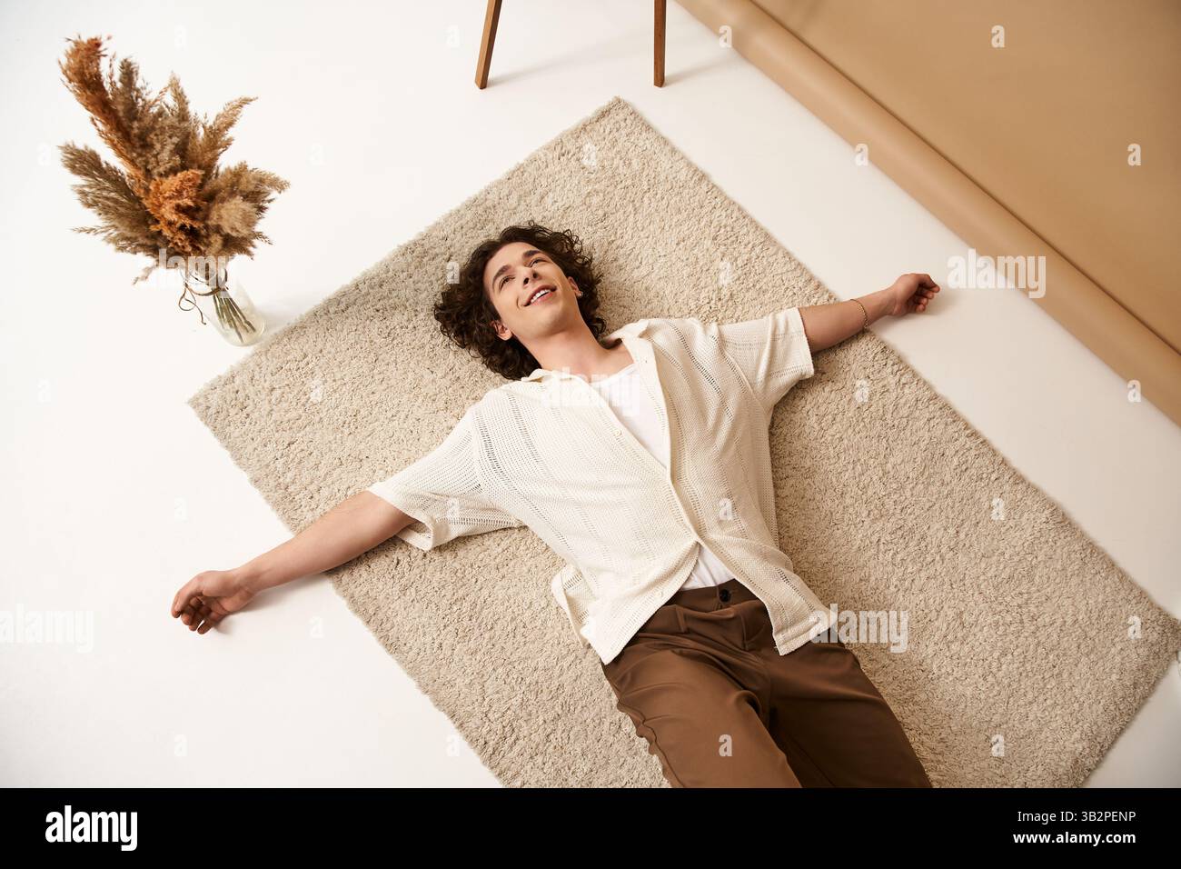 A good looking young man with curly hair lounges on a plush rug ...