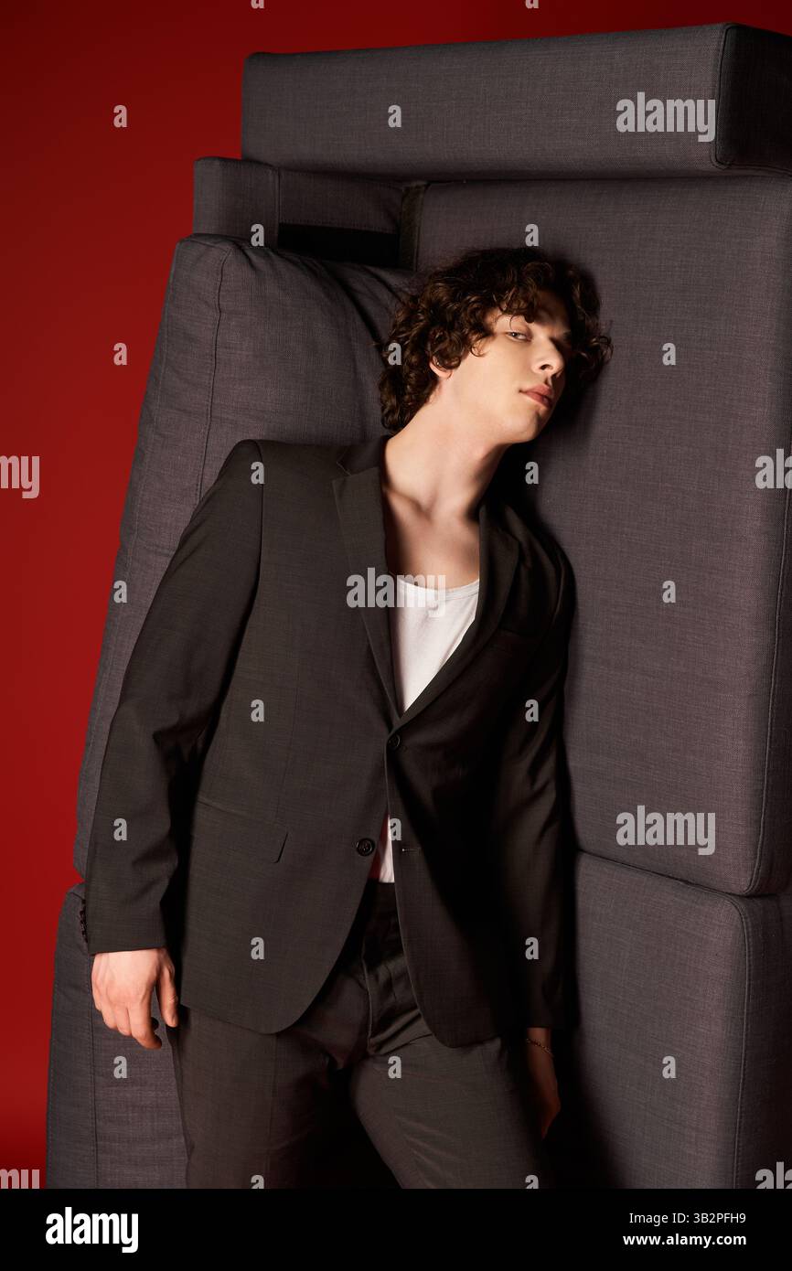 A young man with curly hair leans on grey cushions, flaunting his ...