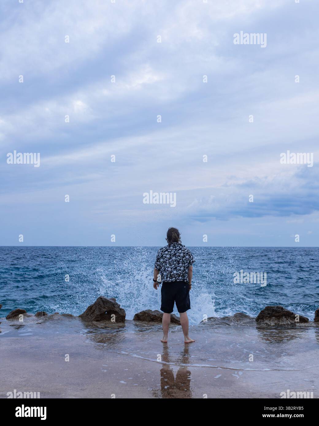 Man in black shorts and shirt walking barefoot on wet concrete pier ...