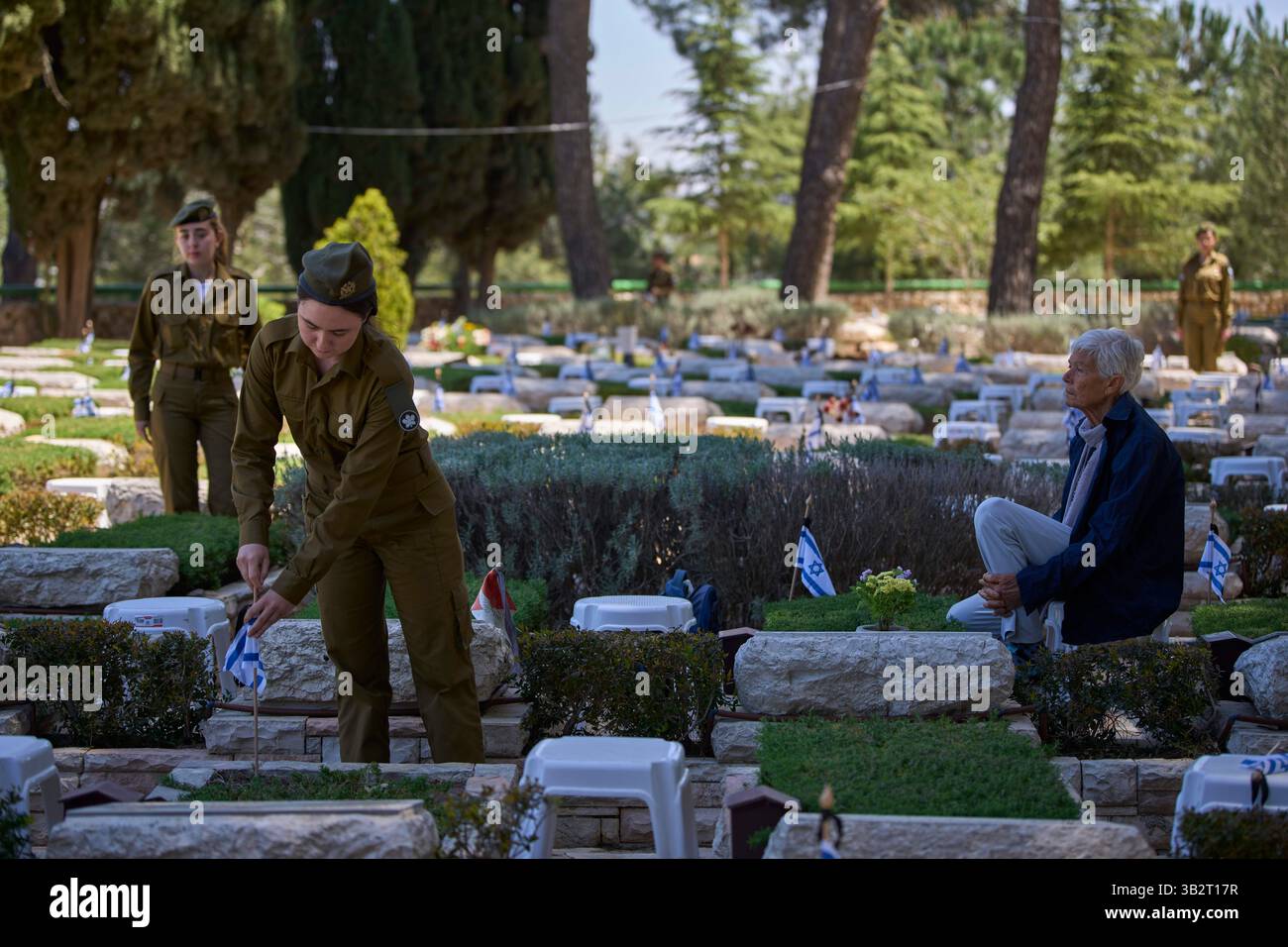 An Israeli soldier places a flag with black ribbons on the grave of a ...