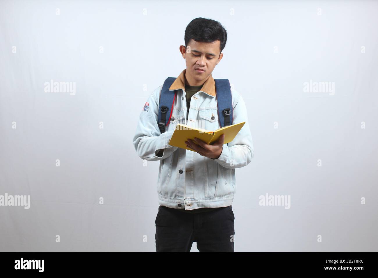student wearing denim jacket carrying bag and reading book seriously ...