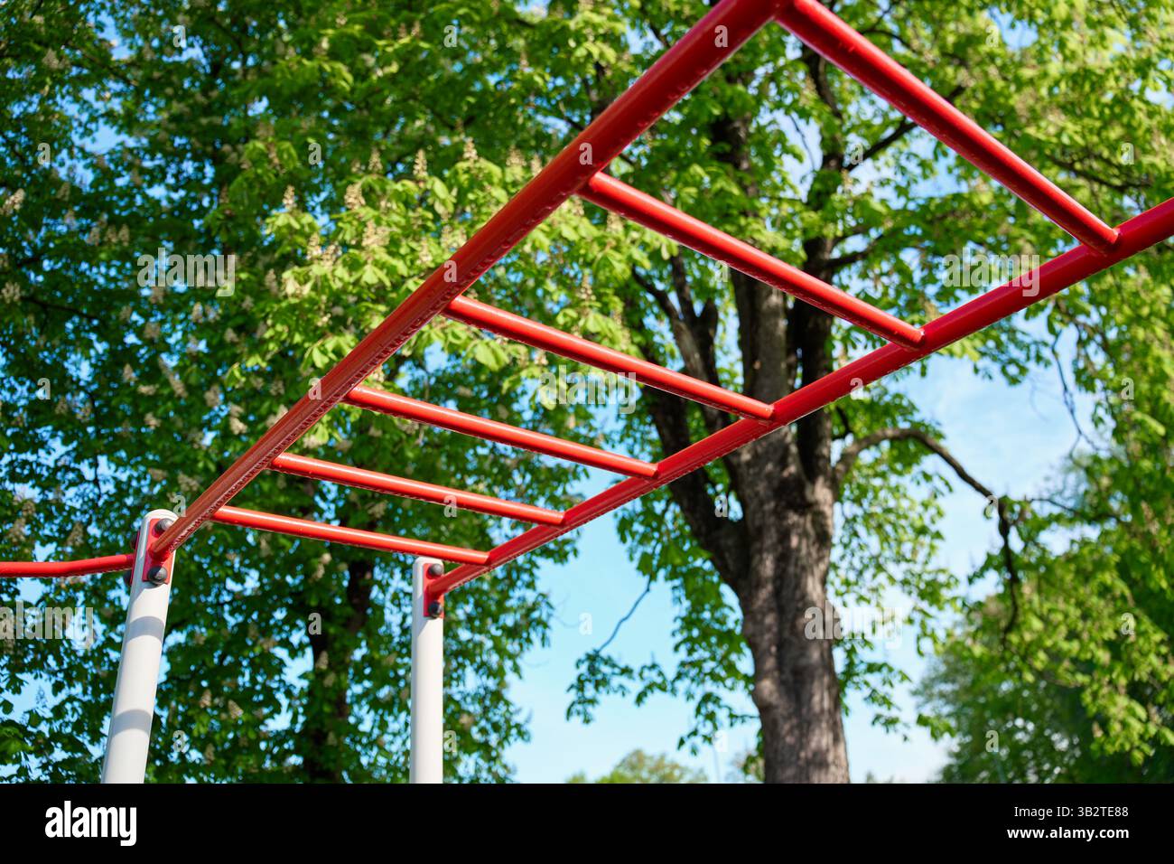 Red outdoor monkey bars in park with green trees. Fitness playground ...