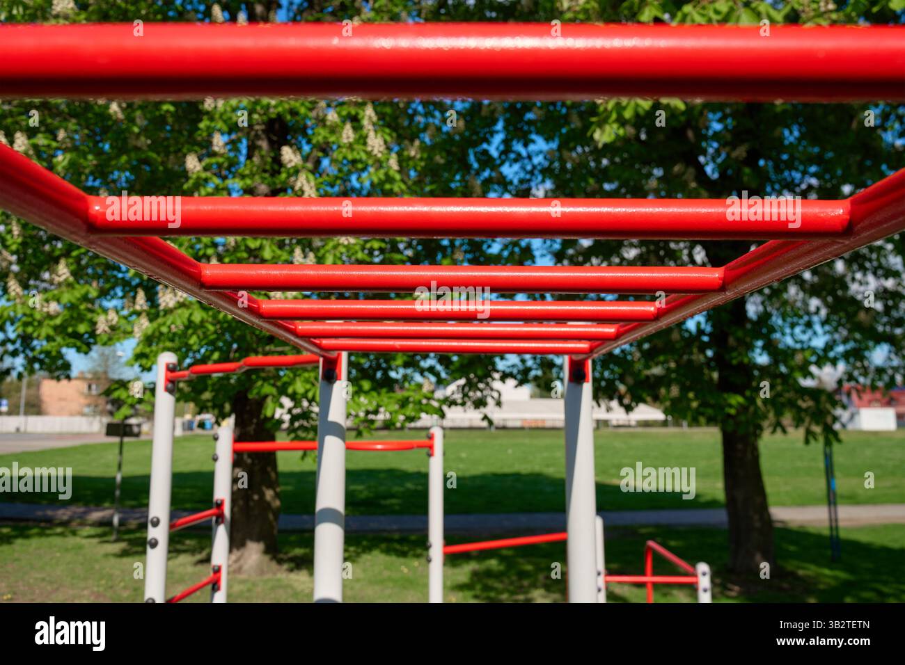Red outdoor monkey bars in park with green trees. Fitness playground ...
