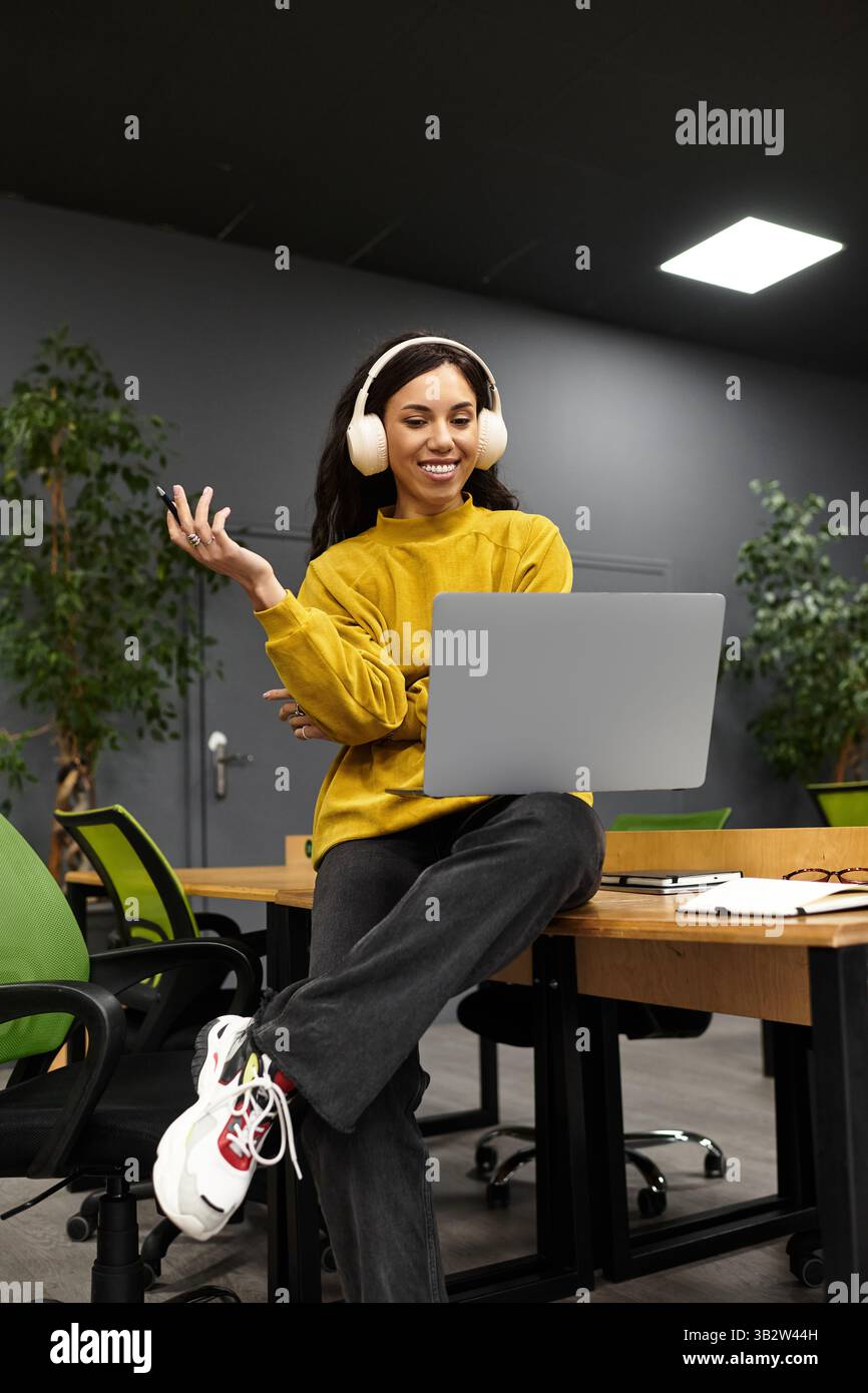 In a lively office, a stylish woman joyfully engages with her laptop ...