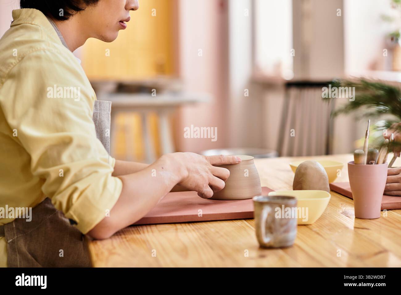 A person shapes clay into a vessel in a vibrant pottery studio packed ...