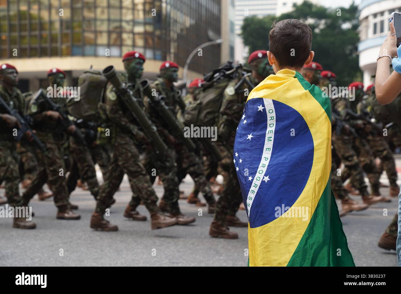 A boy draped in the Brazilian flag watches as troops march past during ...