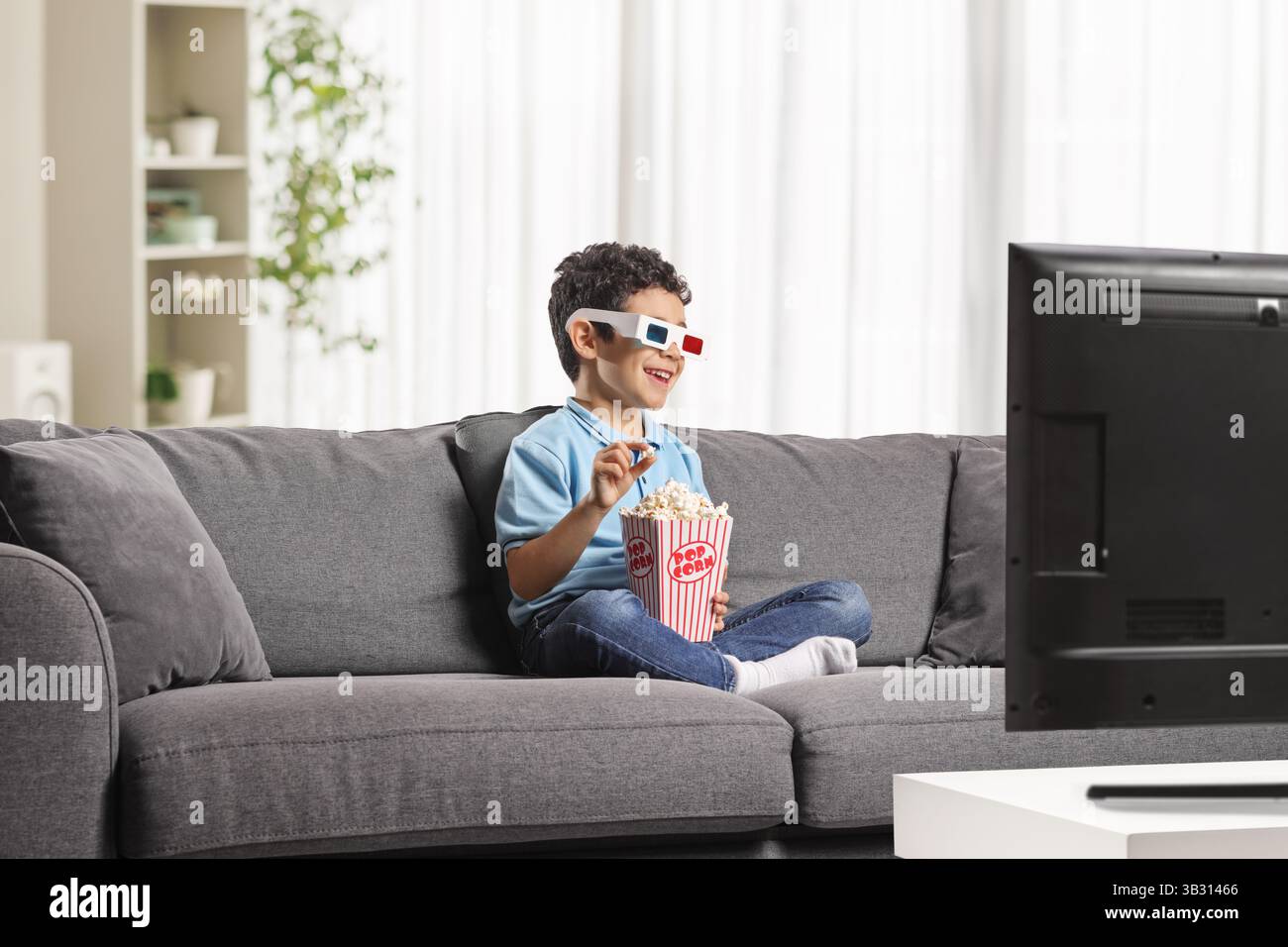 Boy sitting on a sofa watching tv with 3d glasses and eating popcorn ...
