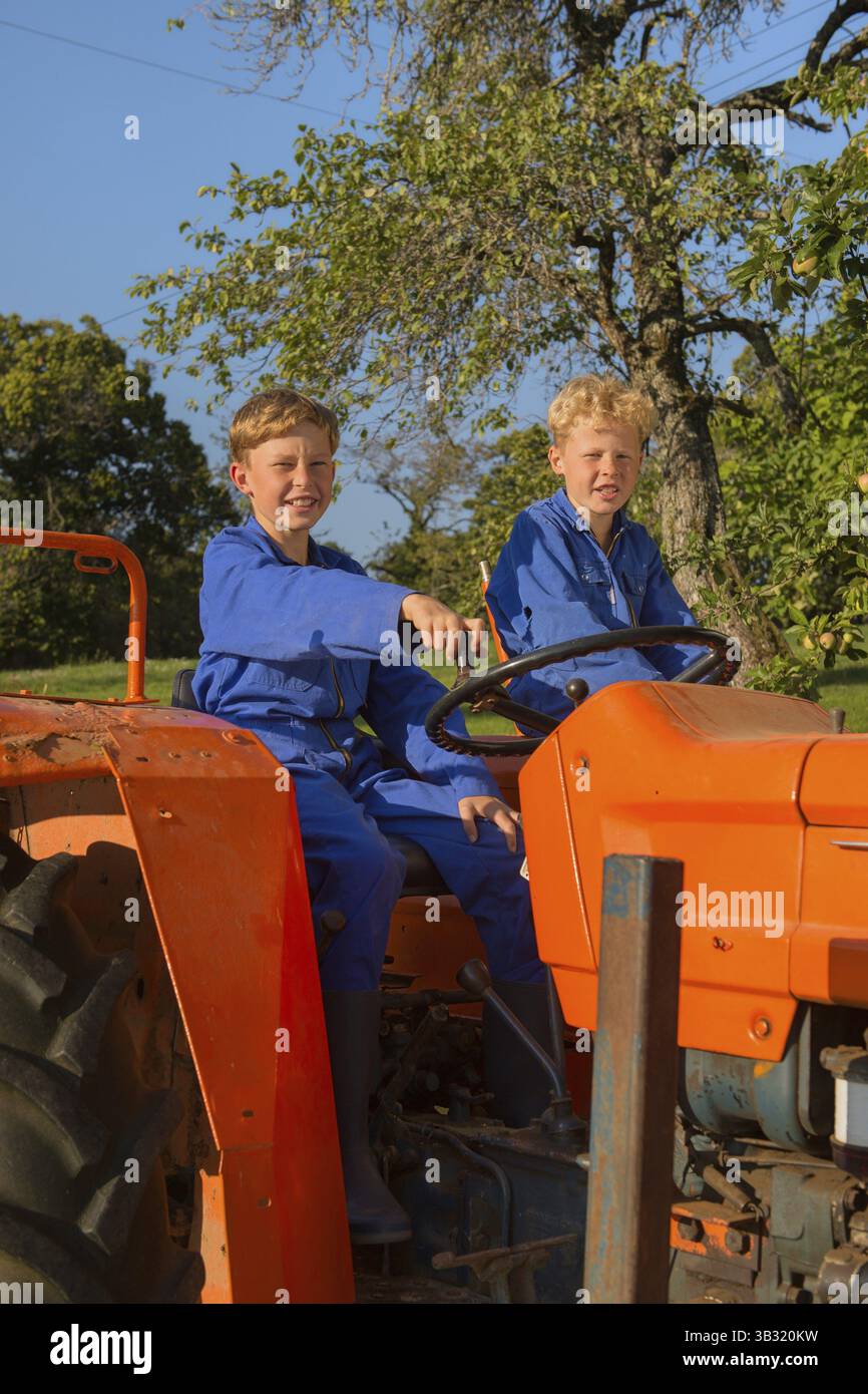 Farm boys riding on orange tractor Stock Photo - Alamy