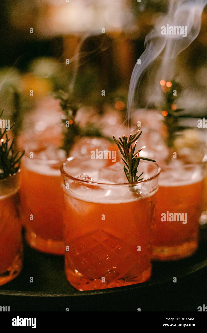 Colorful cocktails with herbal garnishes are served on a tray, creating ...