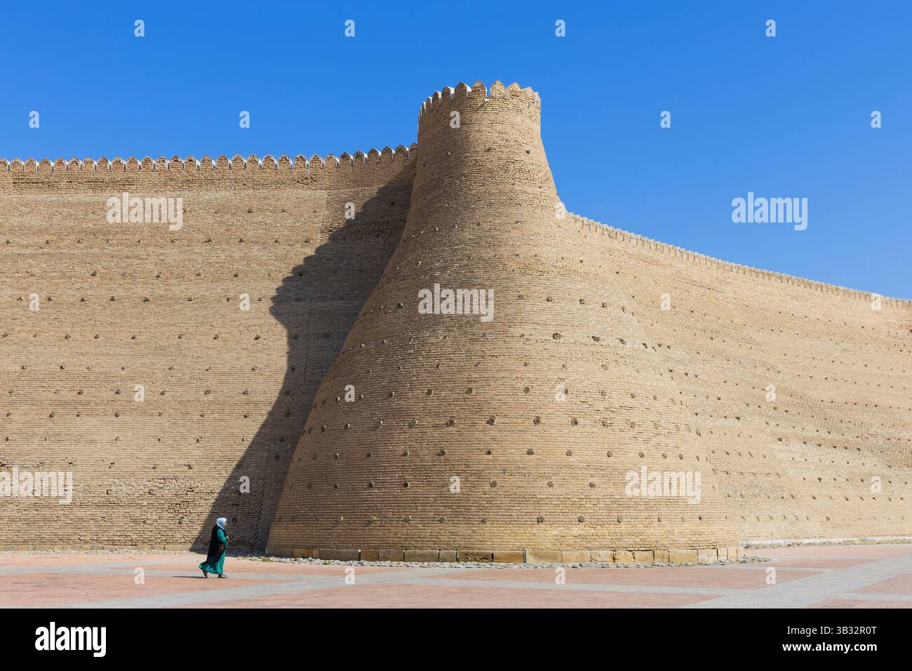 An Uzbek lady in traditional attire walking along the walls of the Ark ...