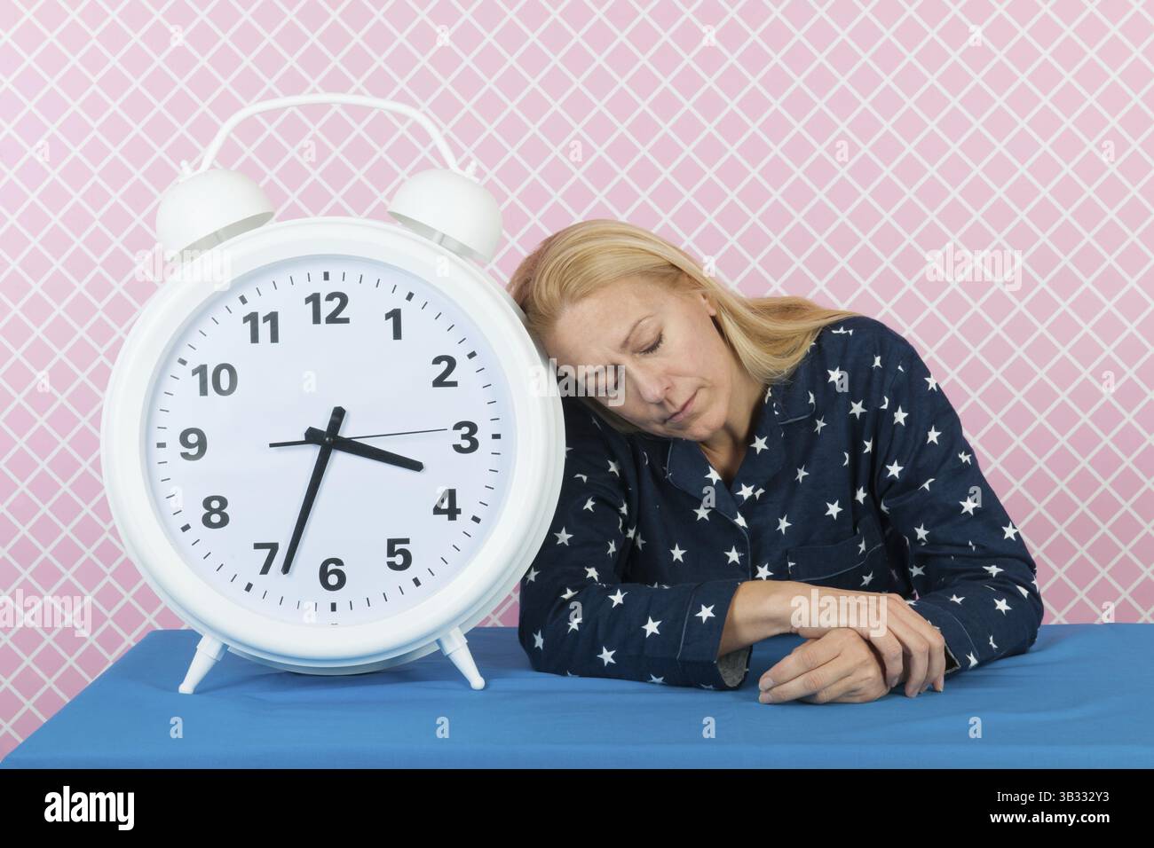 Woman of mature age laying next to big alarm clock Stock Photo - Alamy