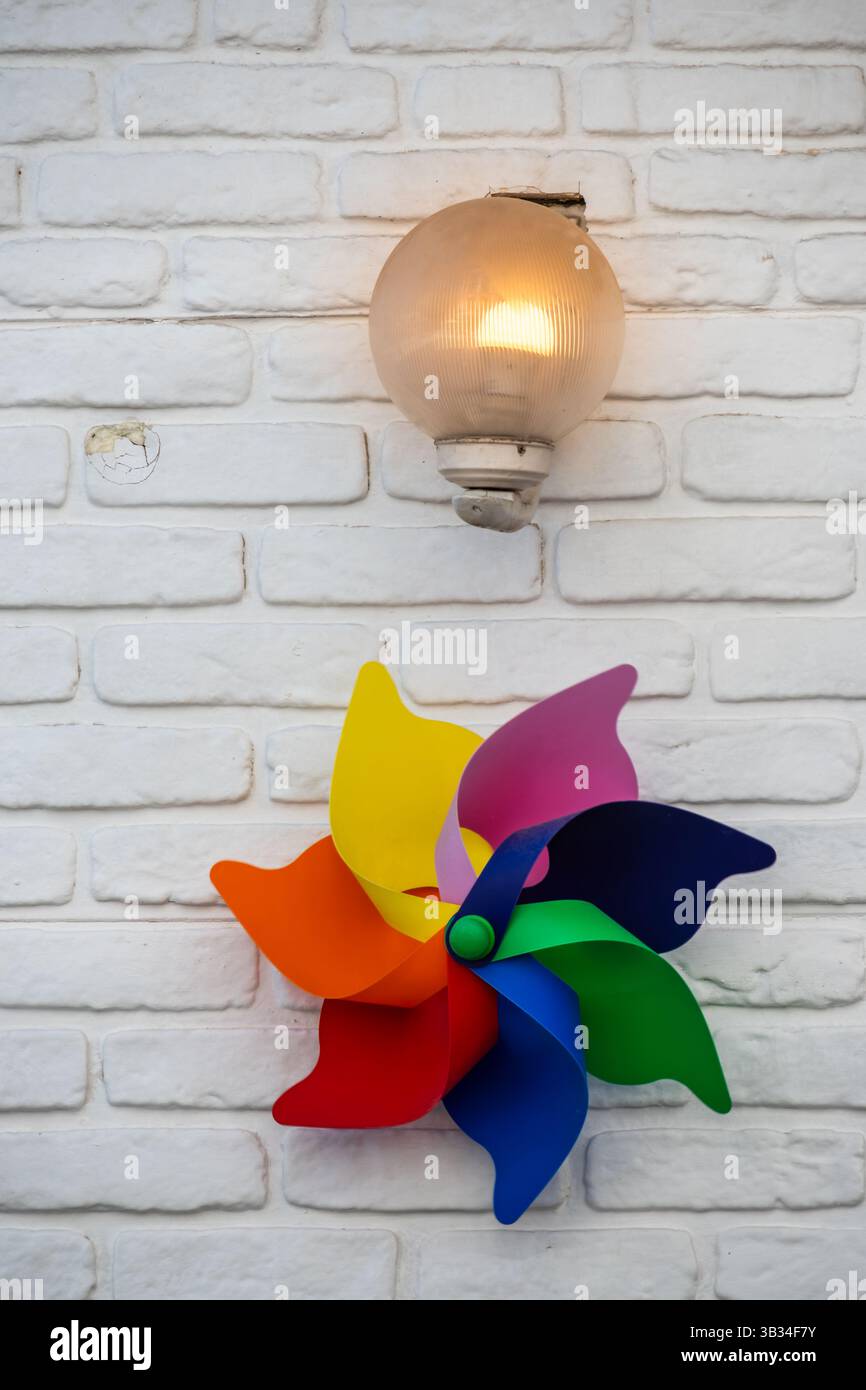 A colorful pinwheel is mounted on a white brick wall beneath a vintage ...