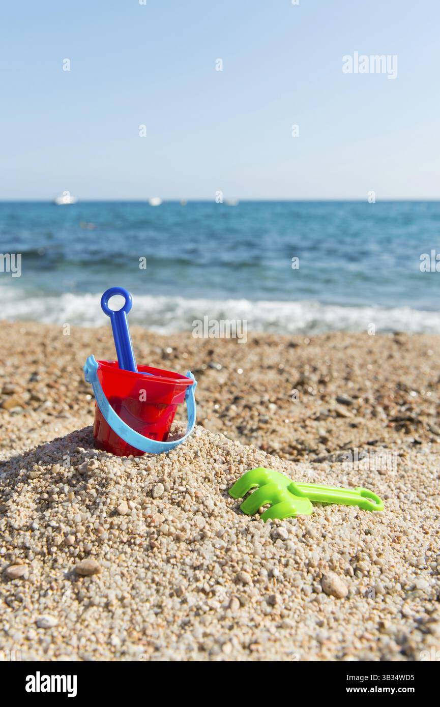 Red plastic toy bucket and rake at the beach Stock Photo - Alamy