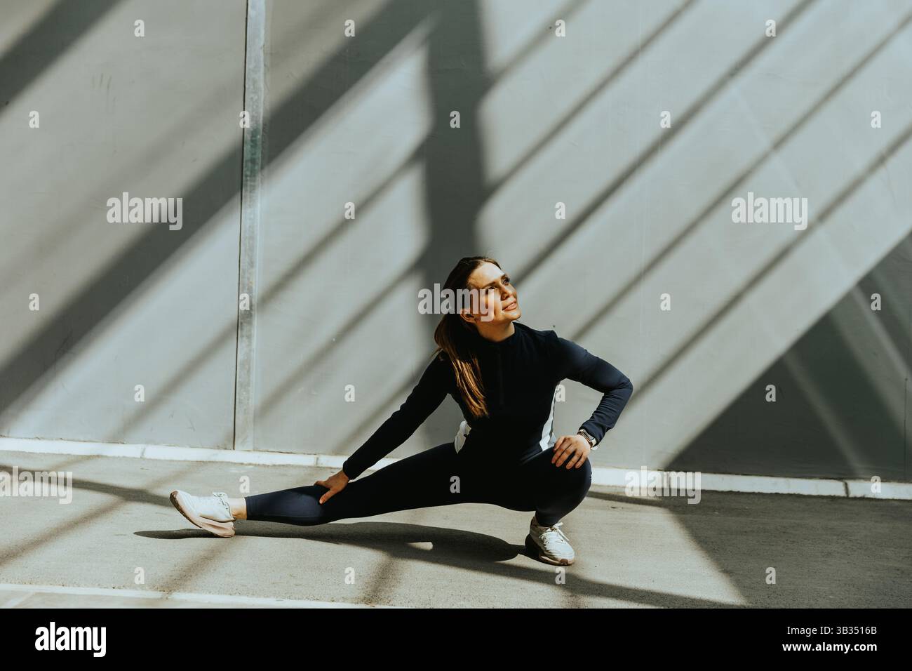 A woman performs a stretching exercise, where dramatic shadows create a ...