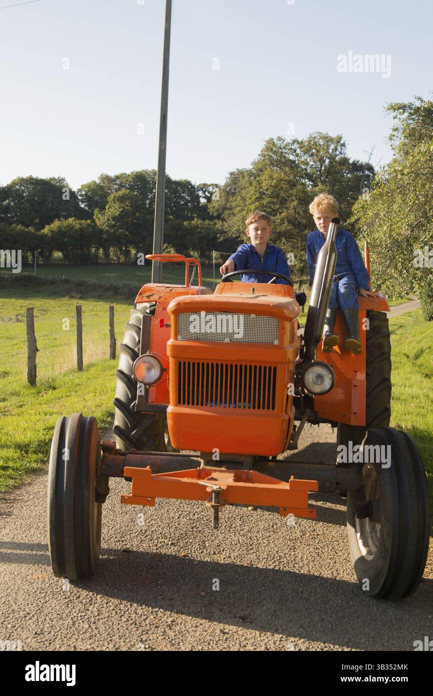 Farm boys riding on orange tractor Stock Photo - Alamy