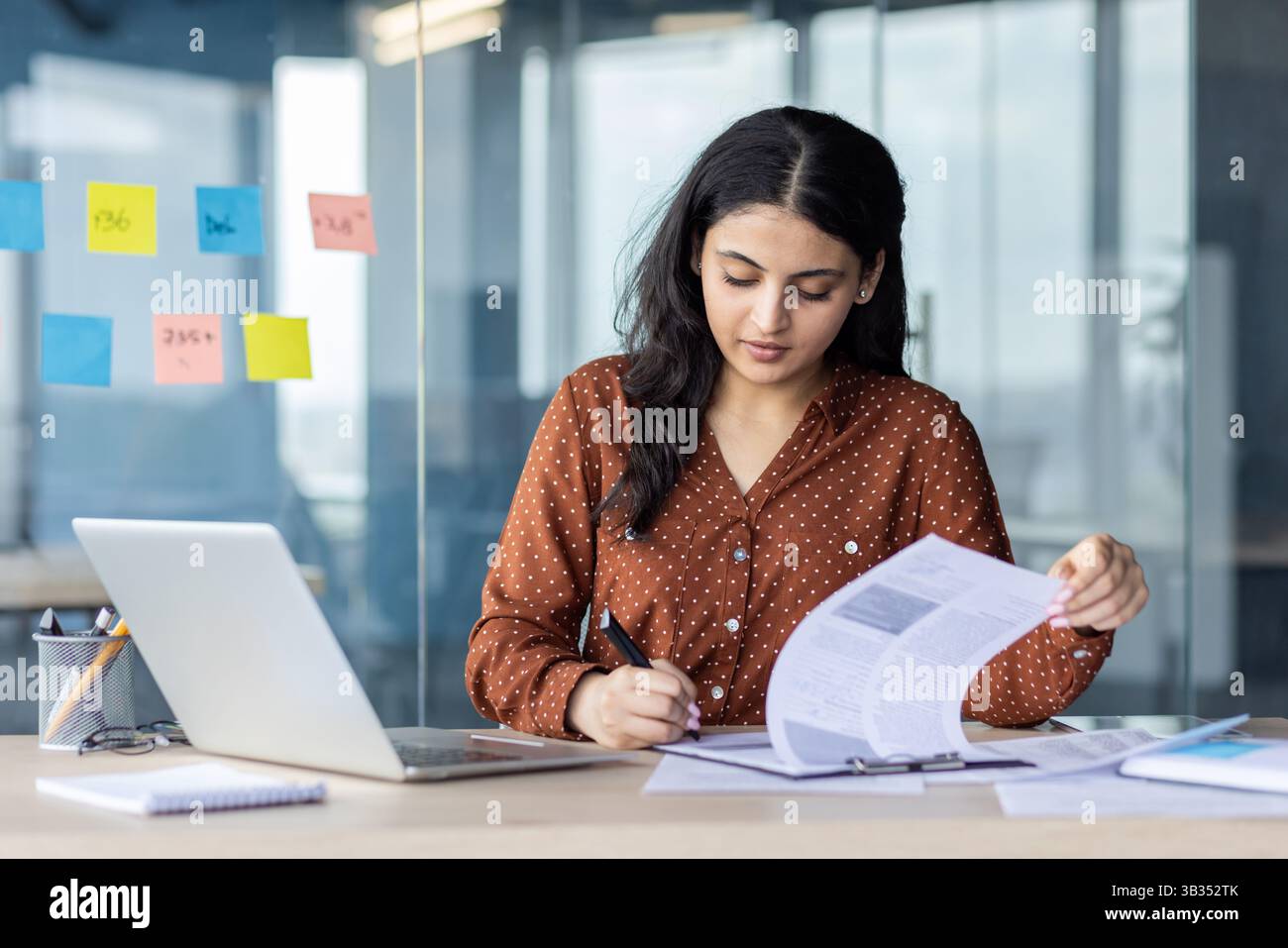 A focused woman, working intently on paperwork at a desk in a modern ...