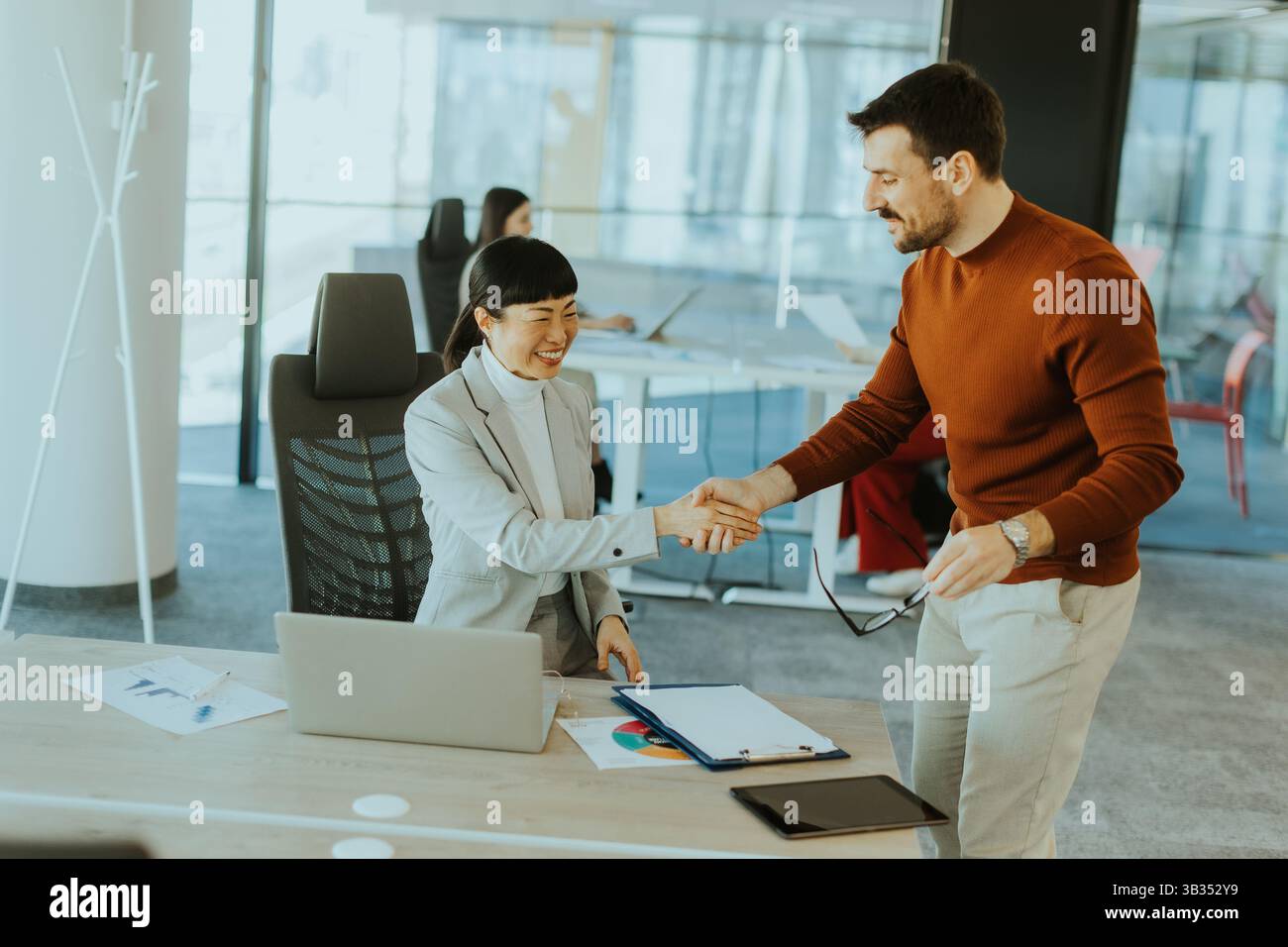 Bright office environment sees a joyful handshake between a male and ...