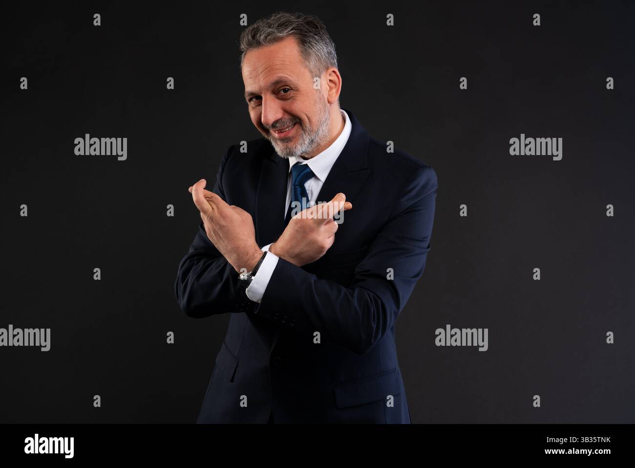 Smiling businessman in suit with arms crossed and both hands showing ...