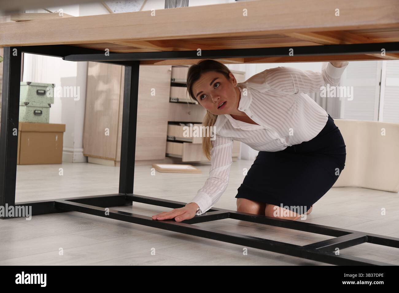 Scared young woman hiding under office desk during earthquake Stock ...