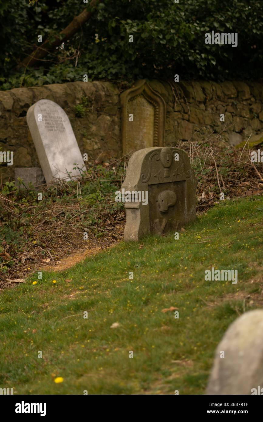 Old stone gravestone partially covered by moss, in a quiet overgrown cemetery with signs of ...