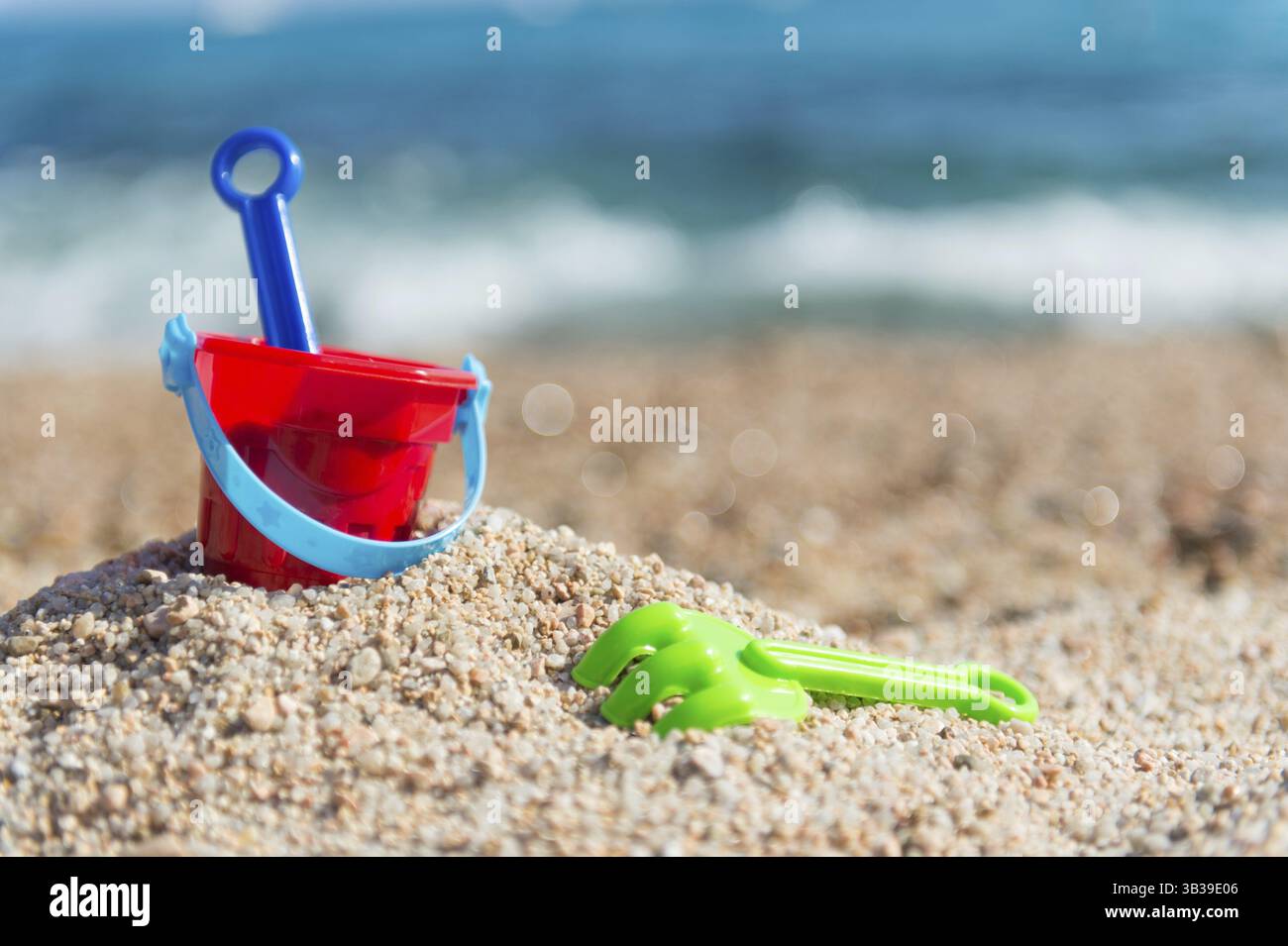 Red plastic toy bucket and rake at the beach Stock Photo - Alamy
