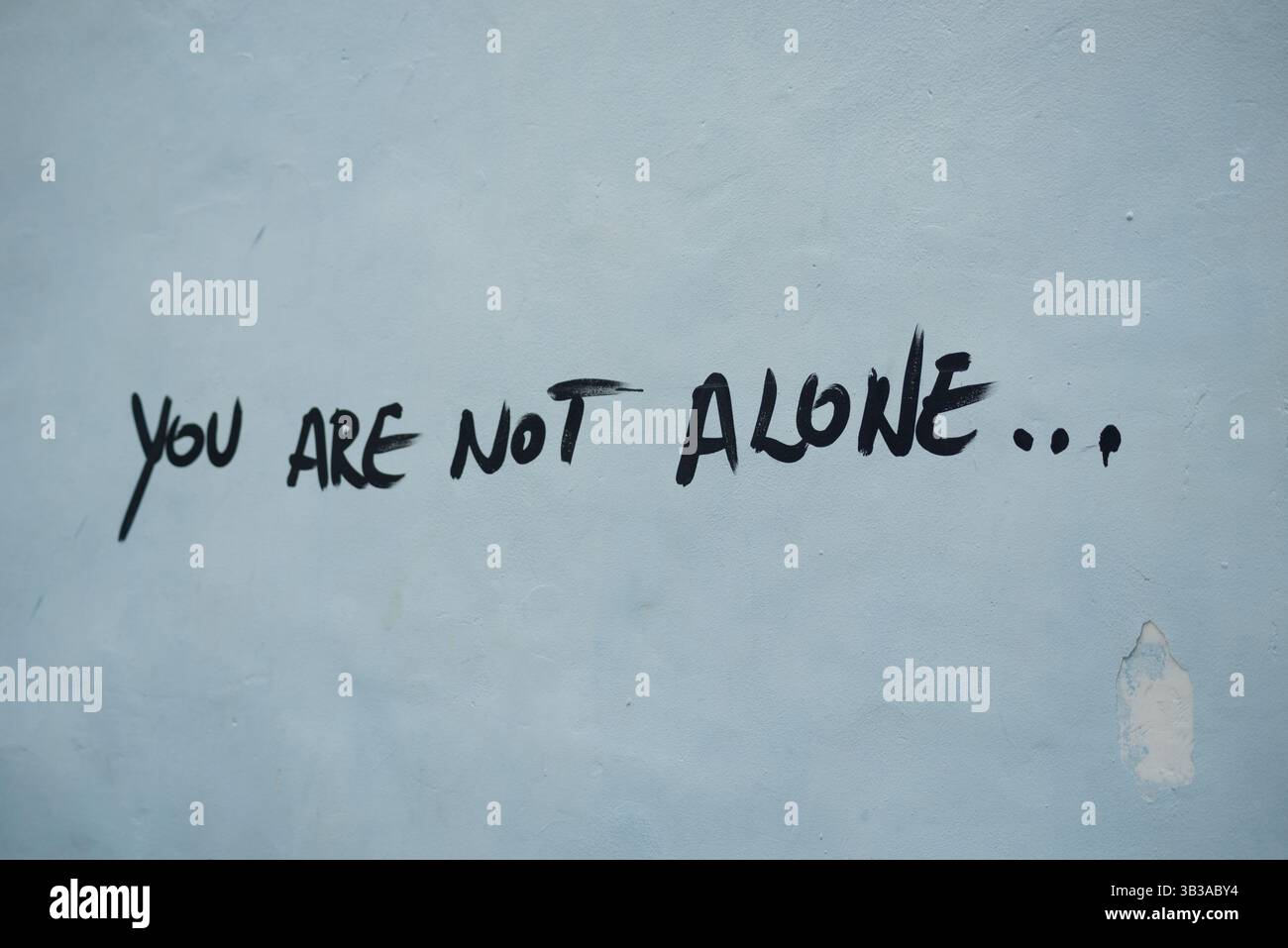 A phrase written on a wall saying you are not alone. Light blue ...