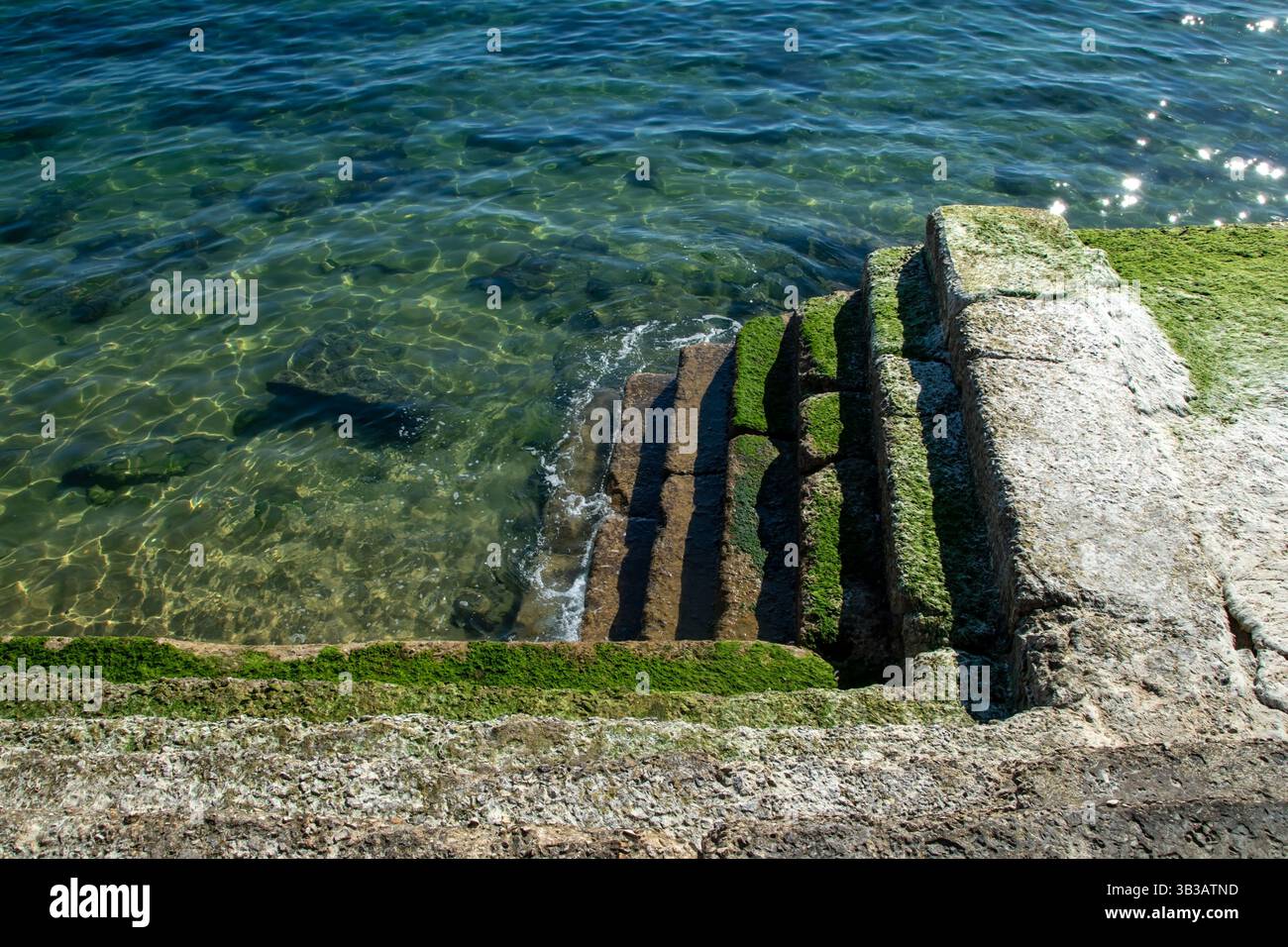 Stone steps covered in green algae lead into clear ocean water with ...
