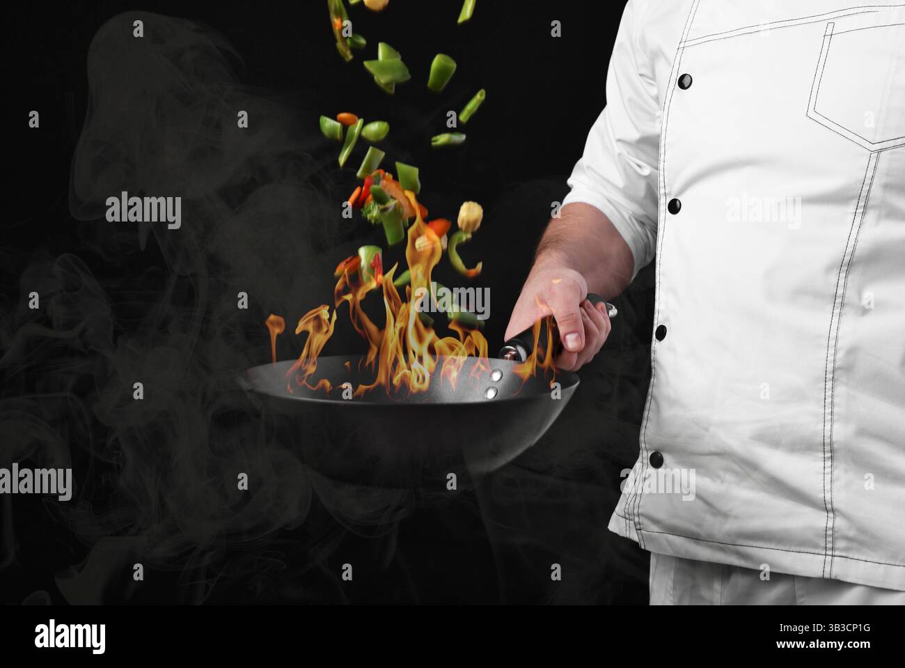 Professional chef tossing vegetables in wok on black background ...