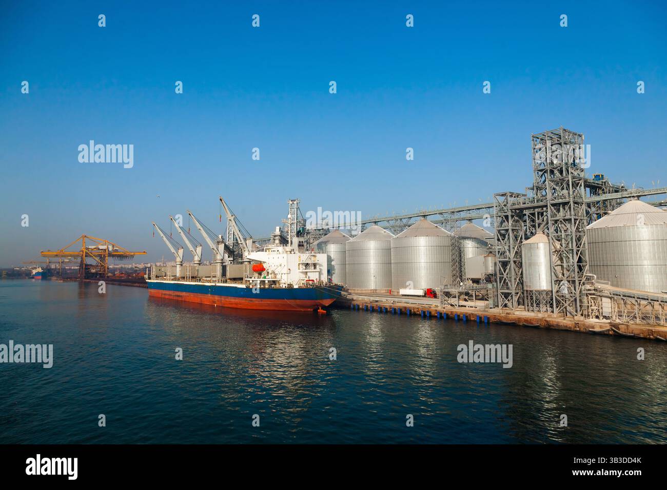 Cargo transport ship is moored at grain storage terminal with storage ...