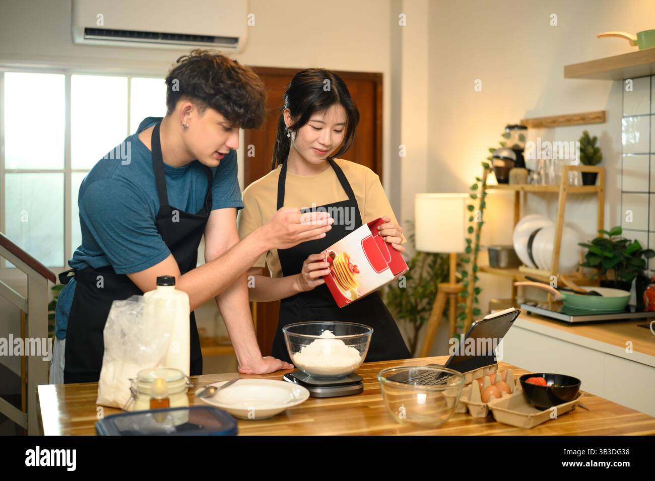 Happy young couple following recipe and measuring pancake mix together ...