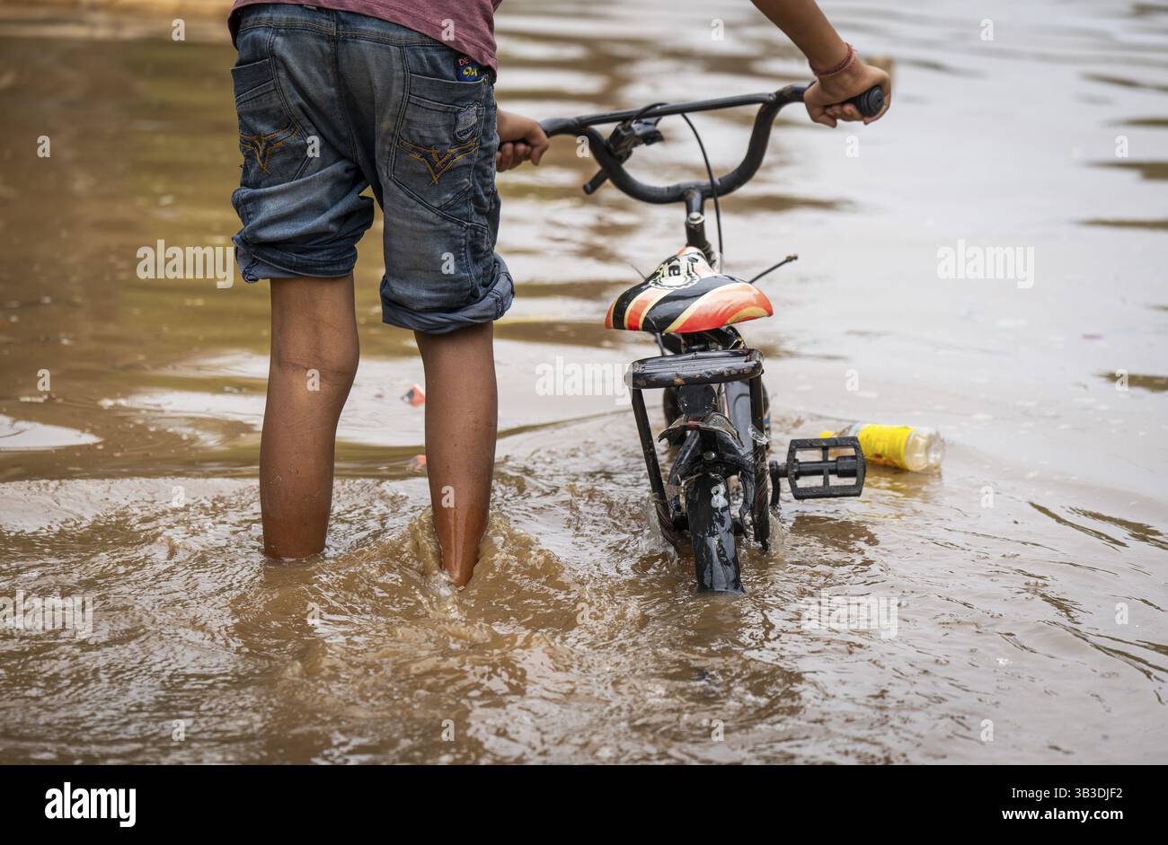 Children wade through a flooded street after heavy rains in Guwahati ...