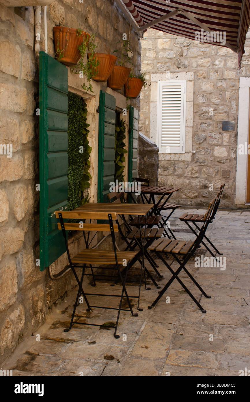 Cozy outdoor cafe setup with wooden tables and chairs, set against aged stone walls and green ...
