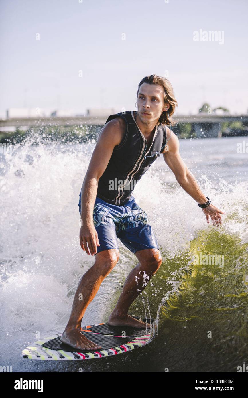 Active wakesurfer jumping on wake board down the river waves. Surfer on ...