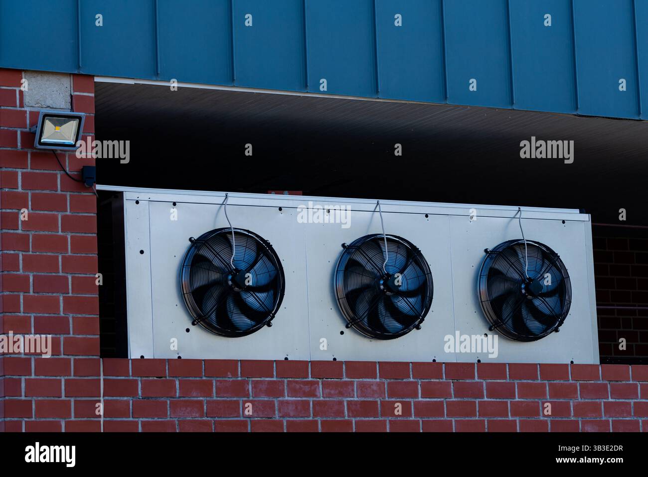 Three large black fans are mounted on a white panel outside a brick ...