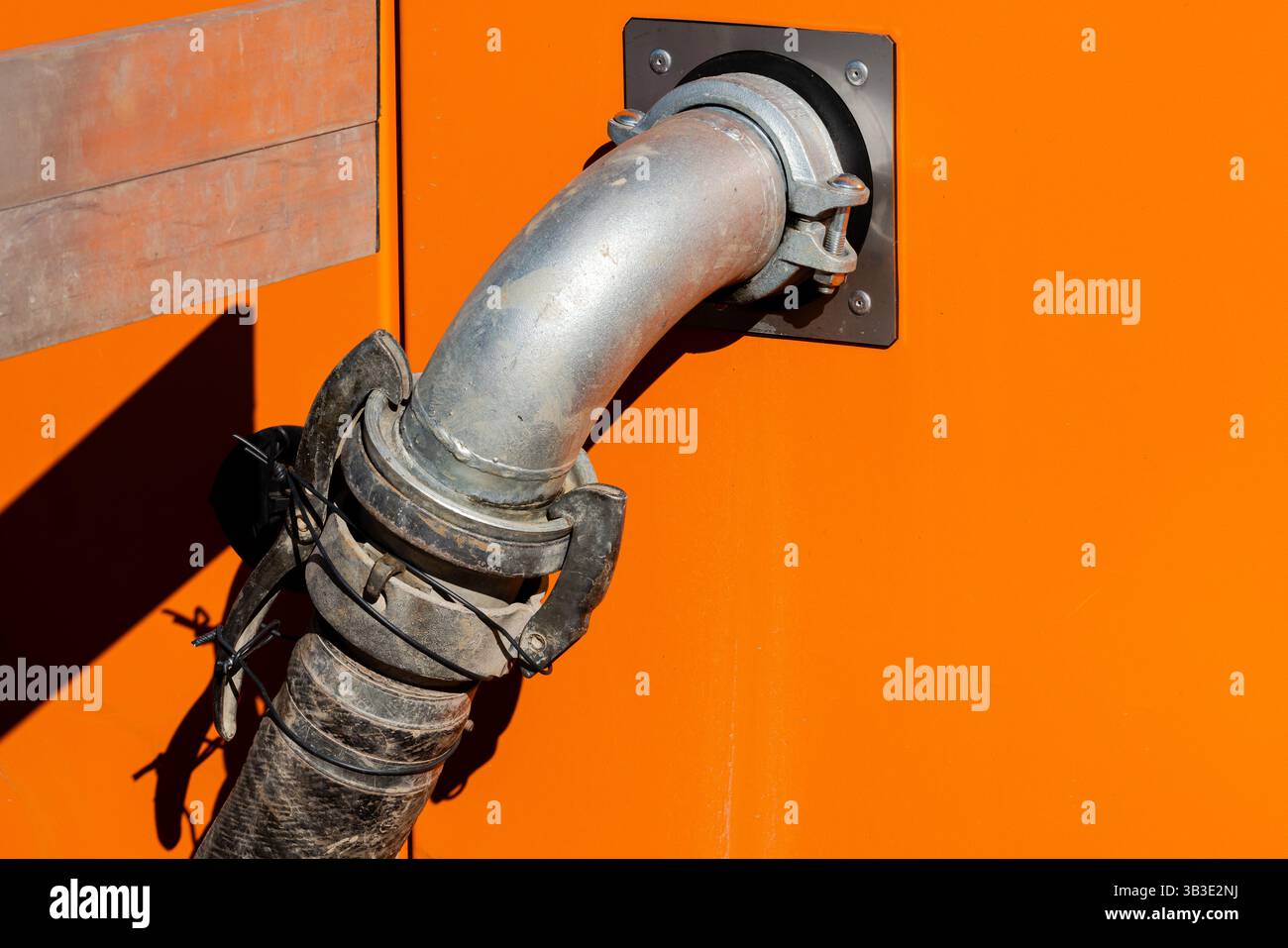 A close-up view of a metal pipe connected to a bright orange tank ...