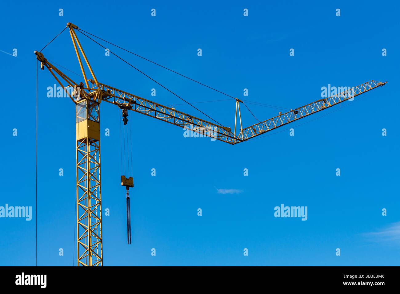 A tall yellow construction crane stands against a bright blue sky ...