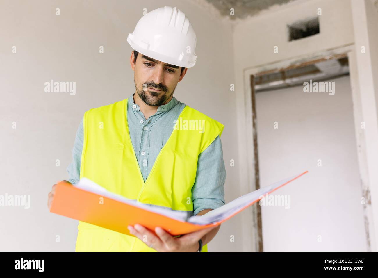 Supervisor wearing hardhat and safety vest checks documents at ...