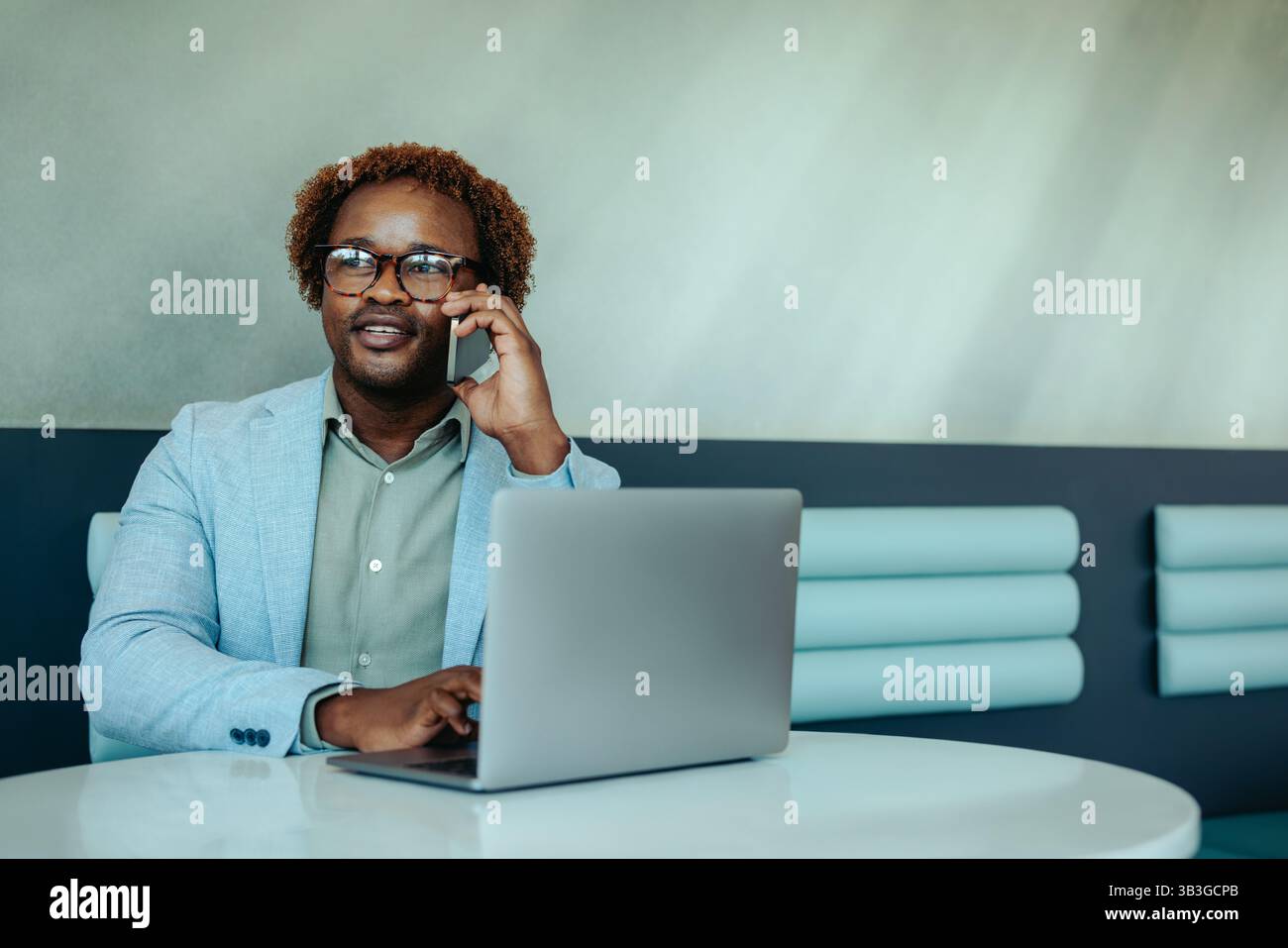 A friendly African salesperson sits at a table in an office setting ...