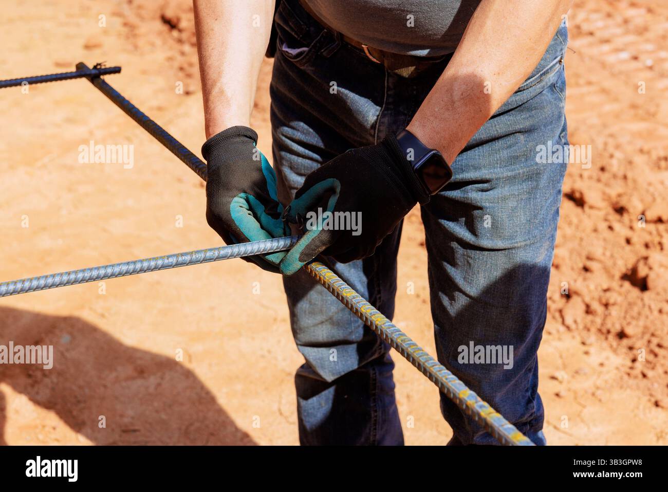 Man in gloves bends rebar with care at construction site, creating ...