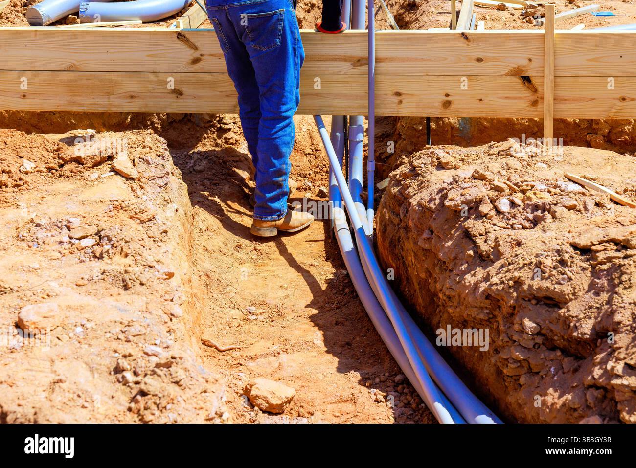 Construction worker positions wooden beams above foundation trench ...